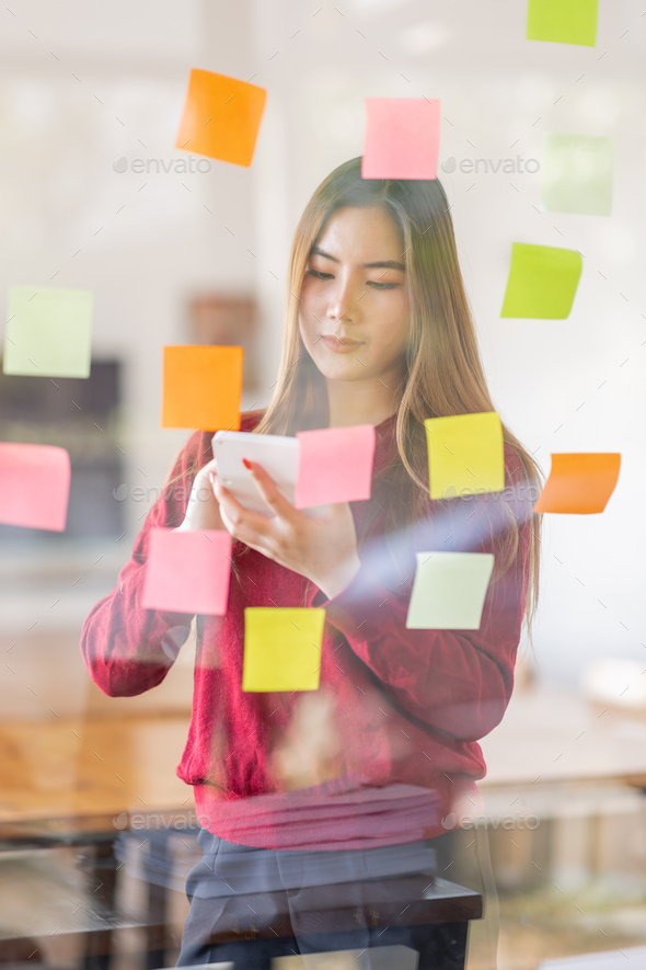 Asian businesswoman creating project plan on office wall with sticky ...