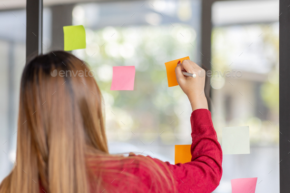 Asian businesswoman creating project plan on office wall with sticky ...