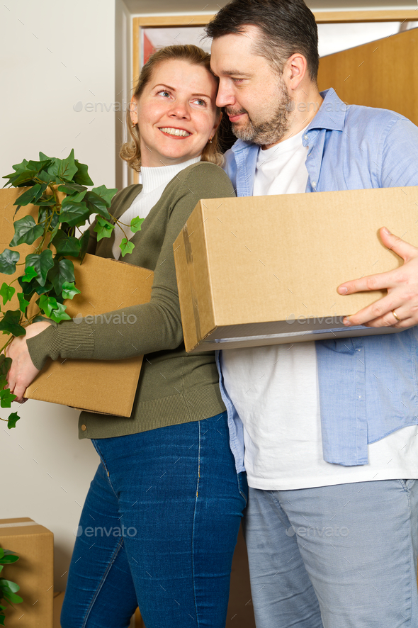 Happy couple moving in their new apartment carrying cardboard boxes ...