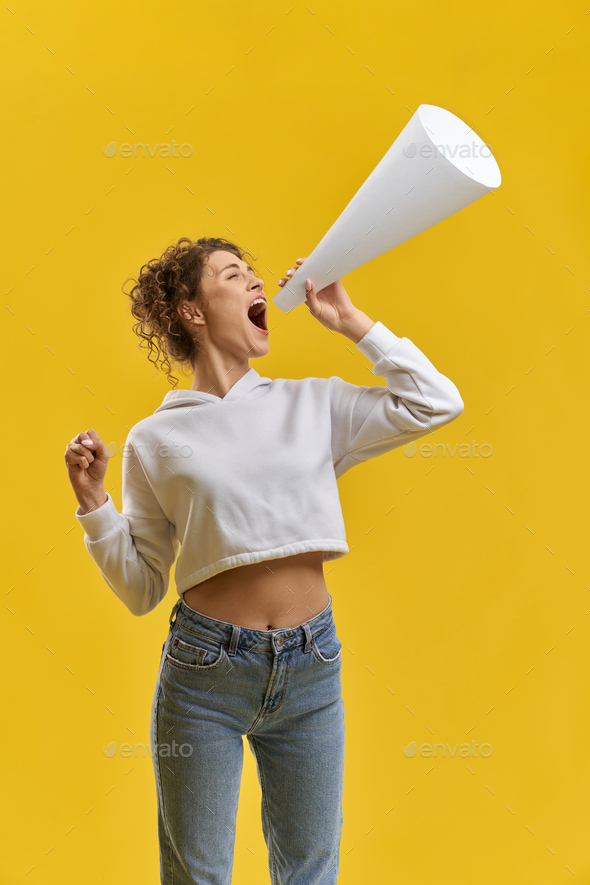Pretty girl standing up with megaphone. Stock Photo by serhiibobyk