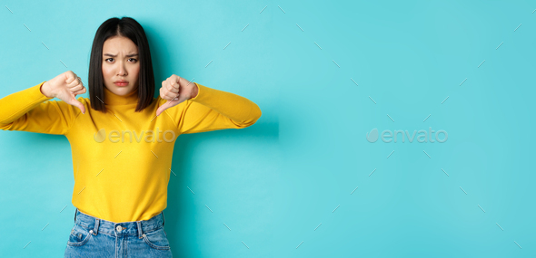 Disappointed asian woman frowning upset, showing thumbs down in dislike ...