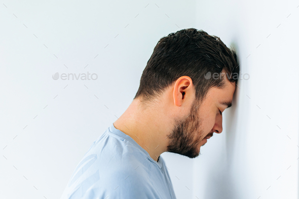 Side view of an unhappy man resting head against office wall. Stock ...