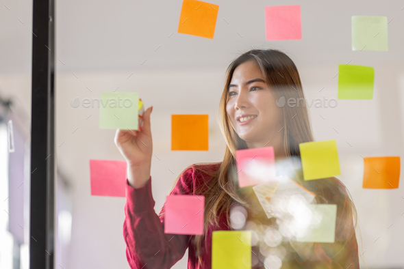 Asian businesswoman creating project plan on office wall with sticky ...