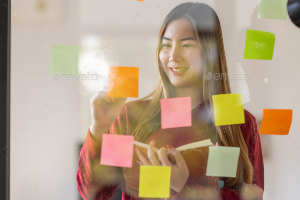 Asian businesswoman creating project plan on office wall with sticky ...