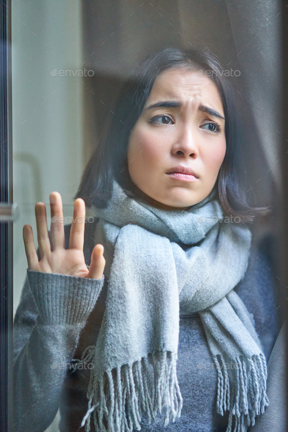 Vertical shot of upset asian woman looking outside, touching window ...