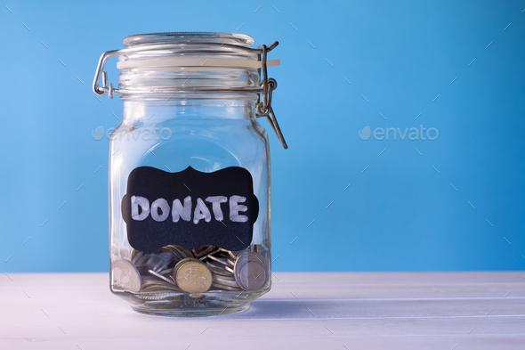 Glass jar with coins with chalk tag Donate on a blue background ...