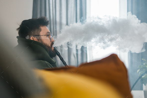Bearded millennial or gen z man smoking hookah while relaxing on sofa ...