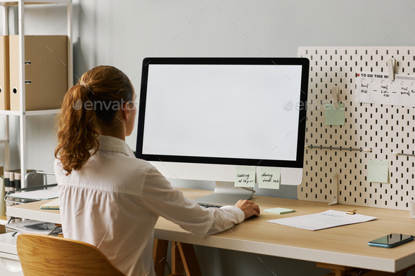Back view young woman using computer with white screen mockup working ...