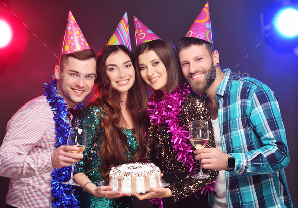 friends in party hats celebrating a birthday holding a cake and glasses ...
