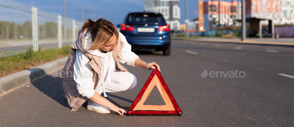 a woman driver puts an emergency stop sign near a broken car, traffic ...