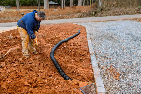 While heavy rainfall is occurring, the worker digs a trench for laying ...