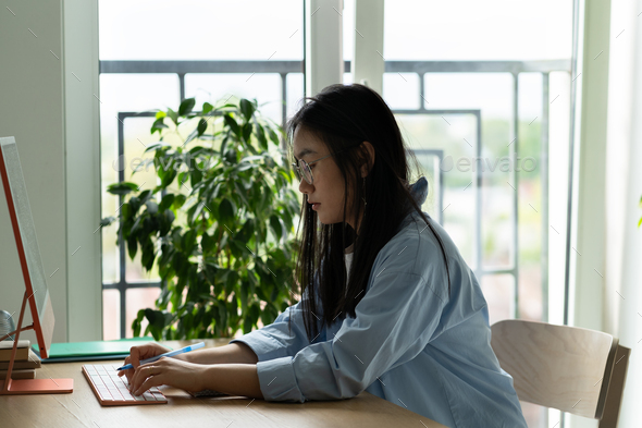 Concentrated Asian girl student in eyewear works home computer on ...
