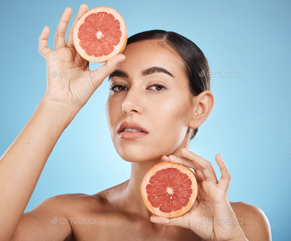 Face, portrait and skincare of woman with grapefruit in studio isolated on a blue background ...