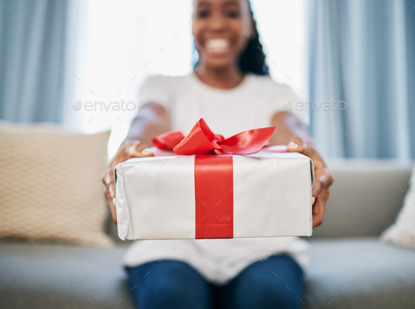 Christmas, gift and a box in the hands of a black woman in her home, sitting on the living room ...