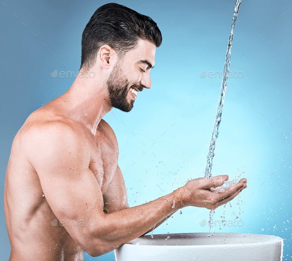 Water splash, skincare and man cleaning hands in studio isolated on blue background for wellness ...