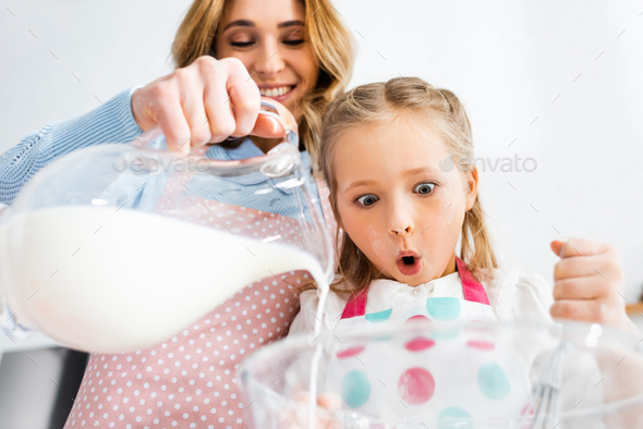 Low angle view of shocked daughter looking at mother pouring milk from ...