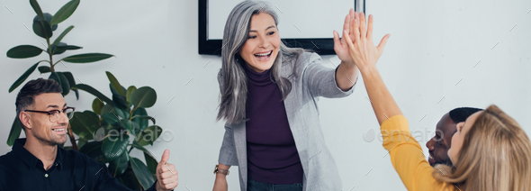 panoramic shot of smiling multicultural colleagues giving high five and ...