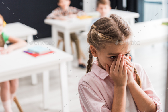selective focus of upset schoolkid crying near classmates, bullying ...