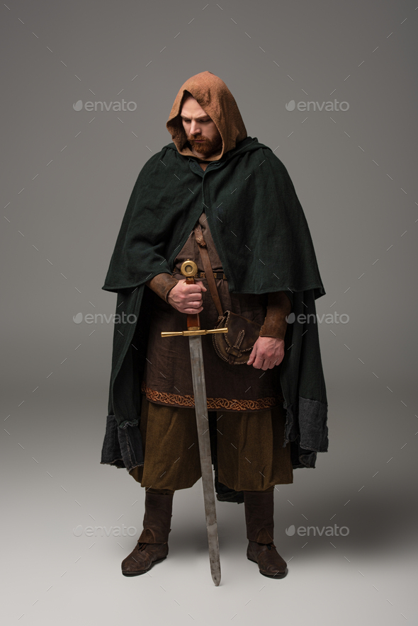 medieval Scottish redhead knight in mantel with sword on grey ...