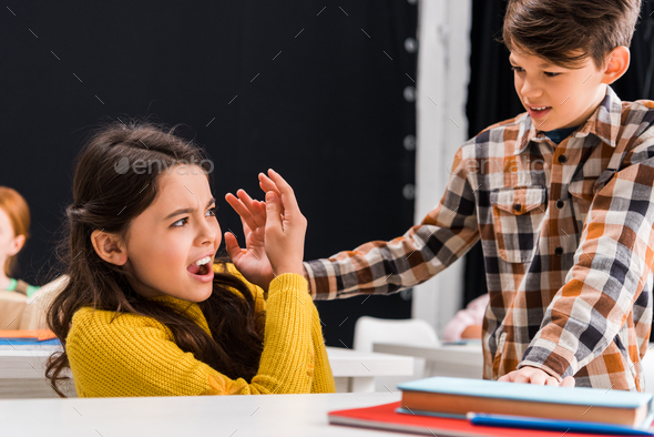 selective focus of cruel schoolboy abusing scared schoolgirl in ...