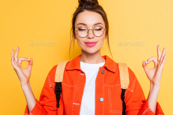 smiling student in eyeglasses standing in meditation pose with closed ...