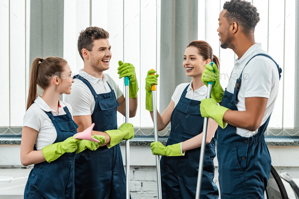 smiling multicultural team of cleaners talking while standing in office ...