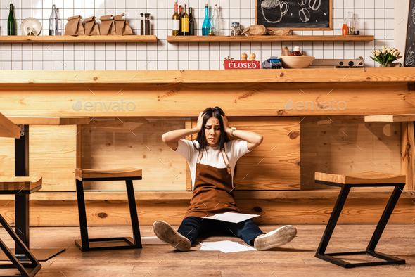 Stressed cafe owner with closed eyes and papers near table and chairs ...