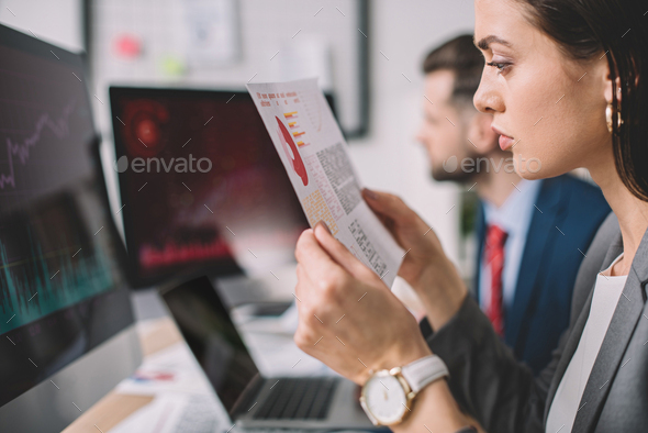 Selective focus of data analyst looking at charts on paper while working with colleague in ...