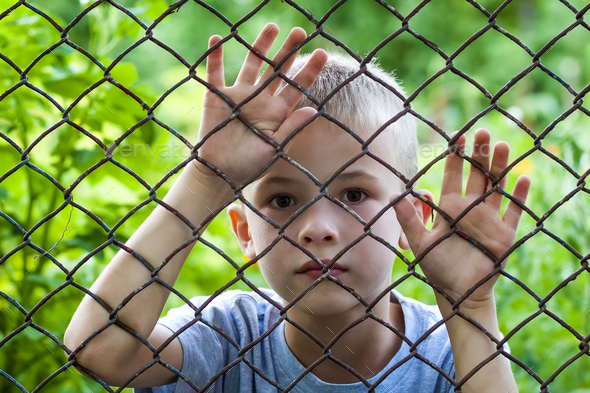 Portrait of a little boy behind chain link fence Stock Photo by bilanol