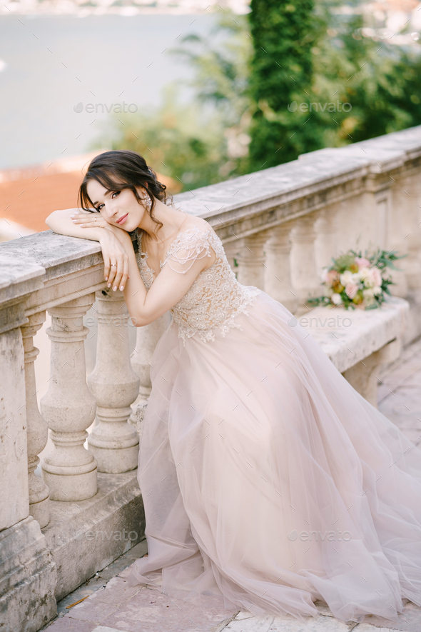 Bride sits on a stone bench with her head resting on a stone balustrade ...