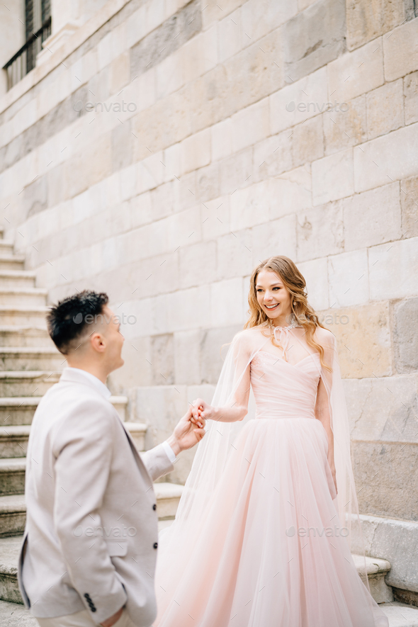 Bride and groom stand holding hands on the steps of an ancient building ...