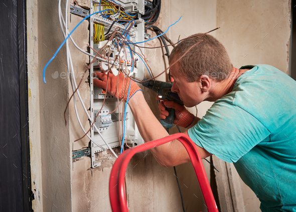 Male electrician repairing electrical panel with power drill. Stock ...