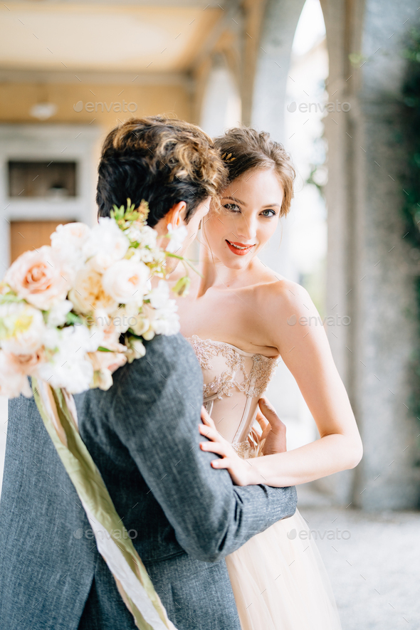 Groom hugs bride with a bouquet of flowers on an old terrace with ...