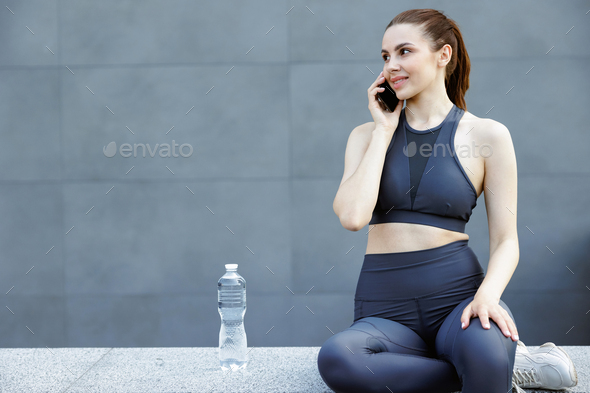 Female fitness trainer talking on phone, while resting after morning ...