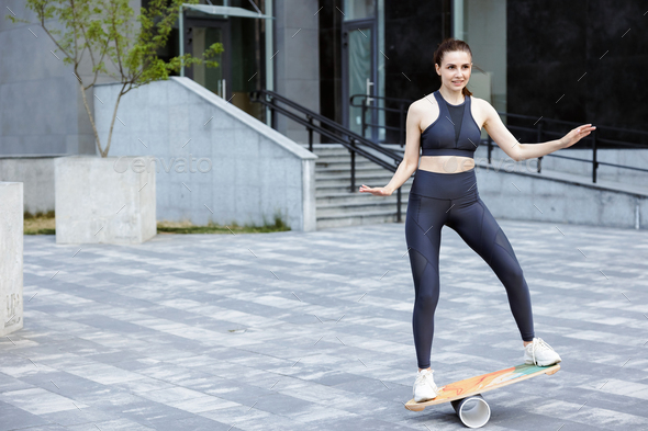Smiling sporty girl having workout with rocker-roller board equipment outdoors. Stock Photo by ...