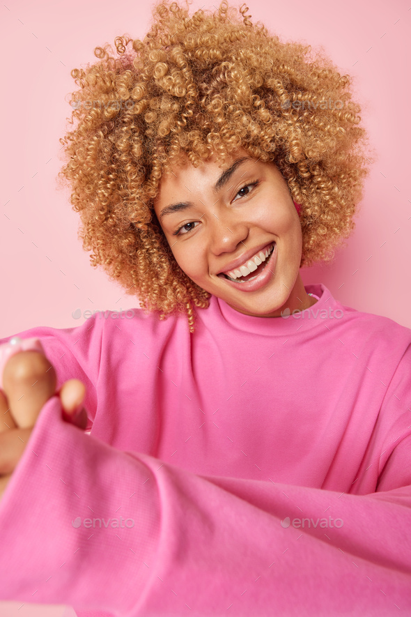 Vertical shot of cheerful curly haired woman keeps hands together ...