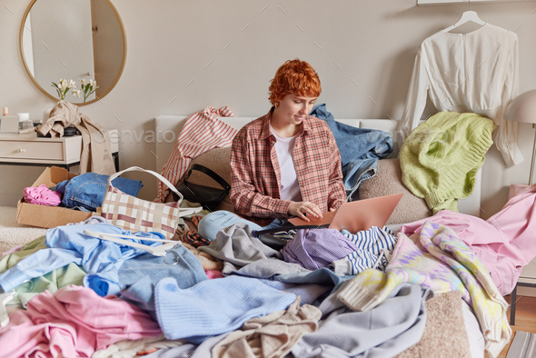 Photo of ginger woman makes revision of clothing at home sits on messy ...