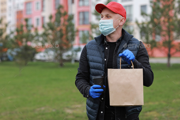Delivery man in red cap, face medical mask, gloves hold take away paper ...