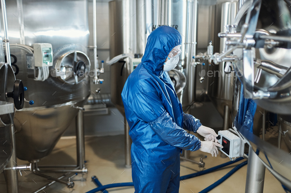 Worker wearing protective suit pressing buttons on equipment in factory ...