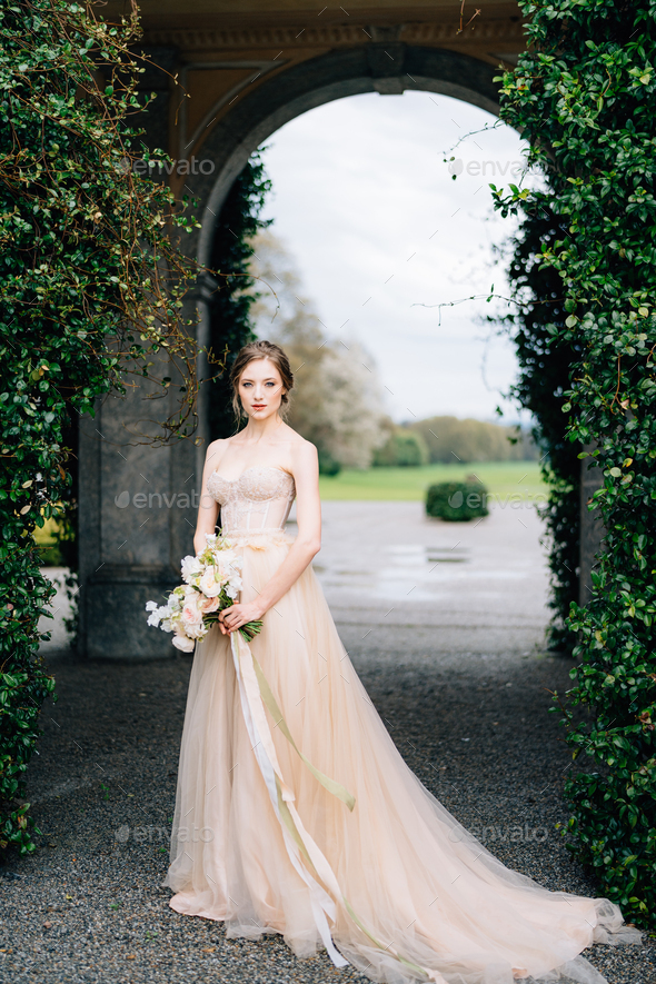 Bride in a long dress holds a bouquet of flowers against the backdrop ...
