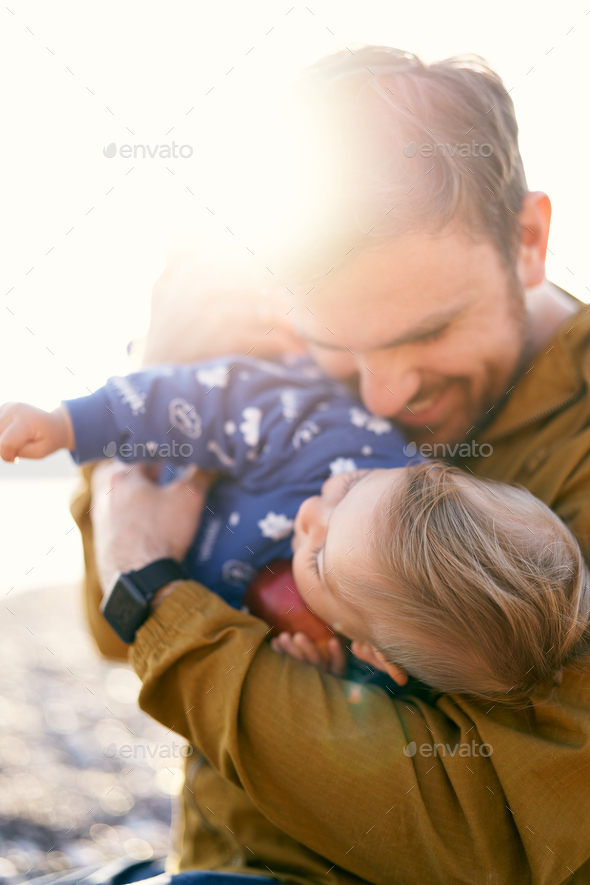 Smiling dad hugs a small child in a blue overalls to his chest in ...