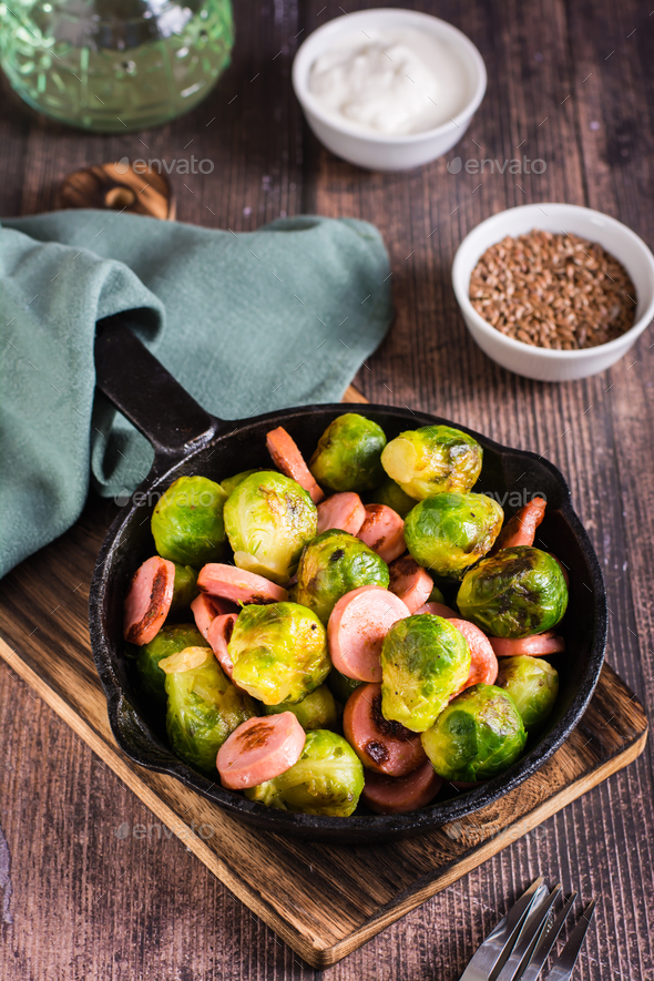 Frying pan with fried sausages and Brussels sprouts on the table ...