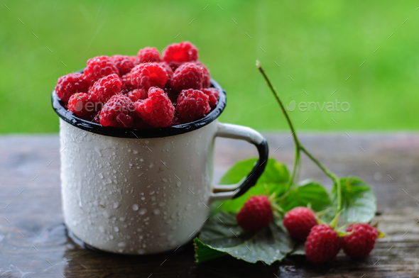 White can and mug with fresh raspberry on rain Stock Photo by molenira