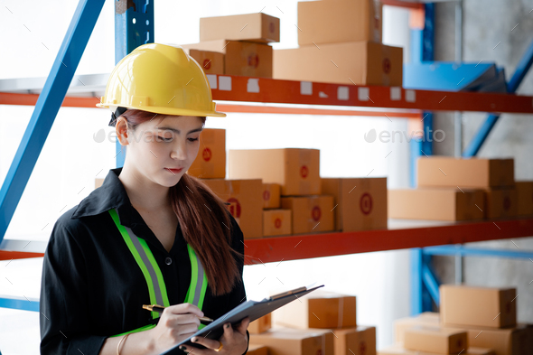 Asian female worker wearing safety clothing is in a warehouse, she is ...