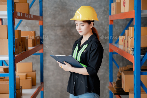 Asian female worker wearing safety clothing is in a warehouse, she is ...