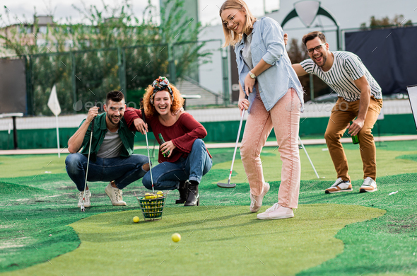 Group of smiling friends enjoying together playing mini golf in the ...