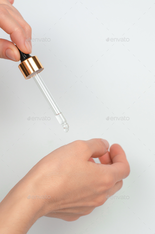 A glass pipette in a woman's hand drips essential oil onto her hand ...