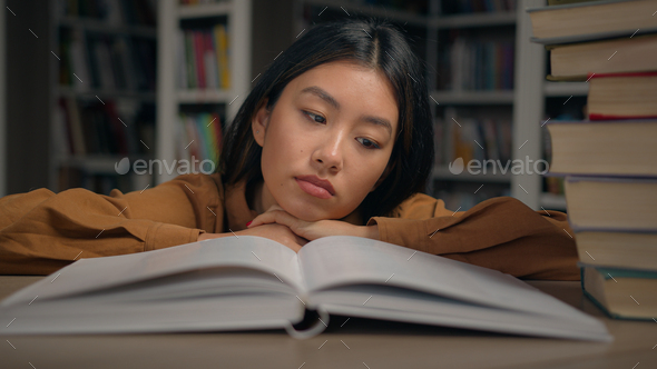 Bored sad tired lazy young korean woman read boring book lying on desk ...