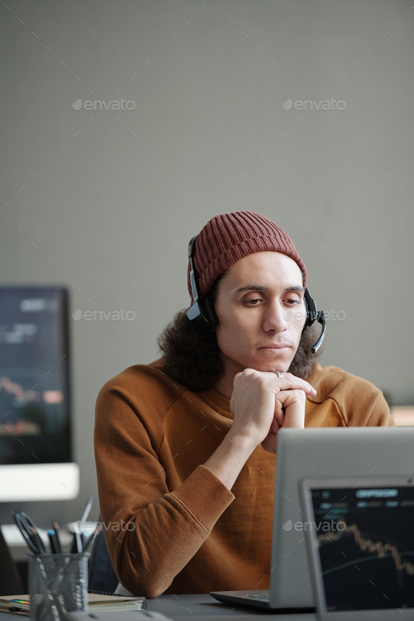 Young serious operator in headset looking at laptop screen by workplace ...