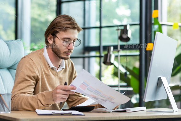 A serious young man accountant, auditor, businessman sits in the office ...